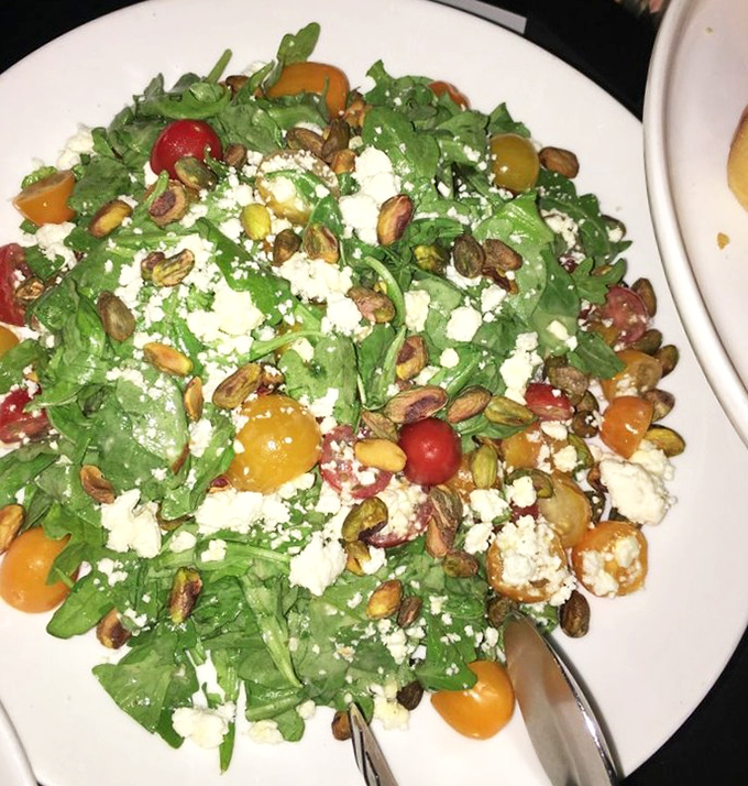 A vibrant arugula salad studded with colorful tomatoes, crumbled cheese, and toasted pistachios that bring crunch to every refreshing bite.