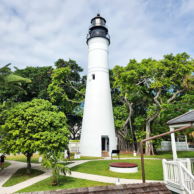 Key West Lighthouse's white tower stands tall amidst tropical greenery, a historic beacon that's witnessed centuries of island life in Florida's southernmost city.