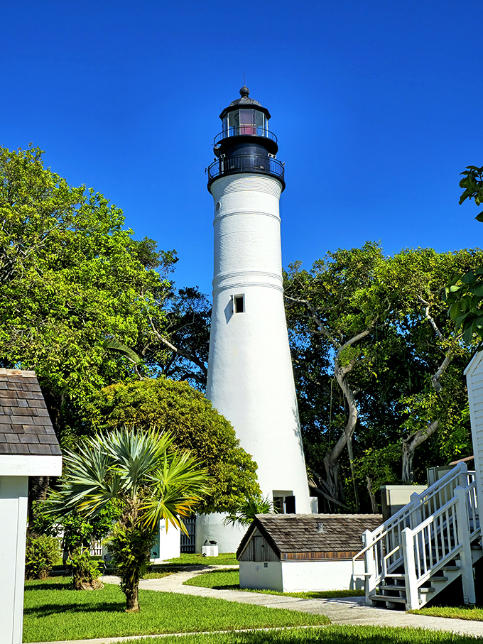 A closer view of Key West Lighthouse shows its simple yet elegant design, surrounded by trees and the lush vegetation that makes Key West so enchanting.