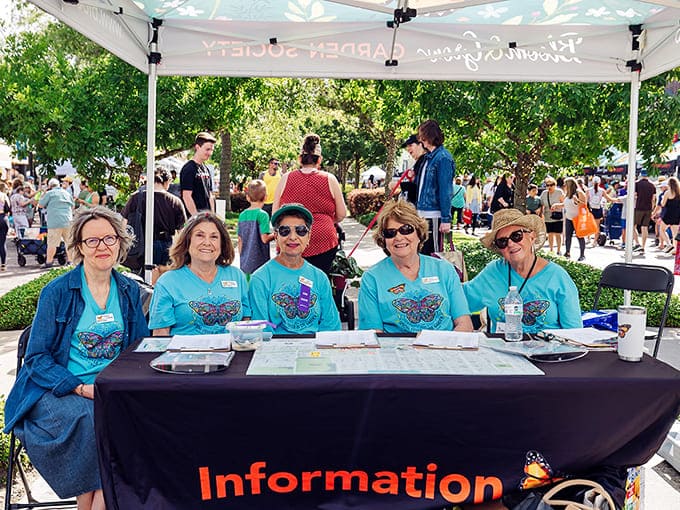 The cheerful volunteer team poses at their information station, ready to guide plant enthusiasts through their botanical shopping adventure.
