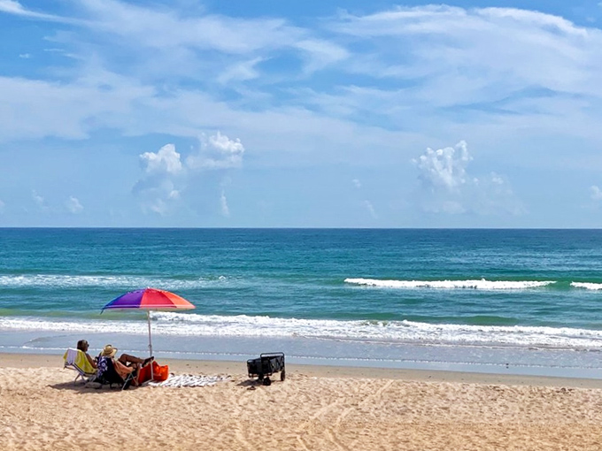 These savvy visitors have mastered the art of seaside relaxation under a rainbow umbrella that screams "vacation mode activated."