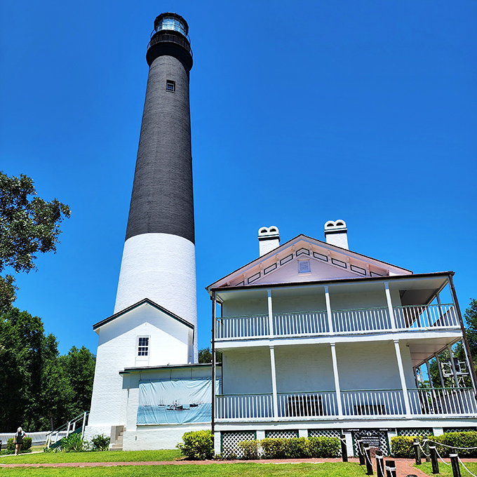 Pensacola Lighthouse's dramatic black and white design creates a striking silhouette against the sky, standing tall beside its historic keeper's house.