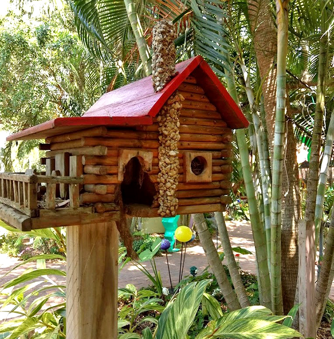 This miniature log cabin birdhouse stands like a tiny wilderness retreat, where feathered guests check in for five-star accommodations among the palms.