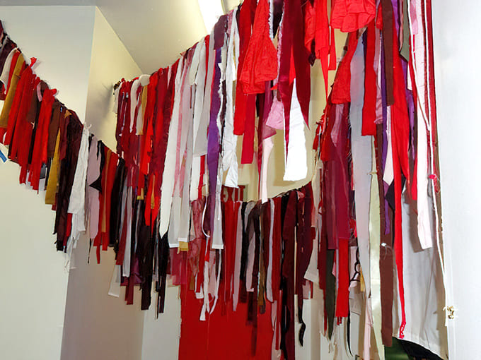 Fabric strips create a birth flag installation, each piece representing a story of bringing life into the world.