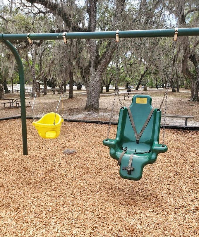 Playground swings hanging beneath ancient oaks create memories where simple joy meets timeless beauty, no batteries required for this kind of fun.