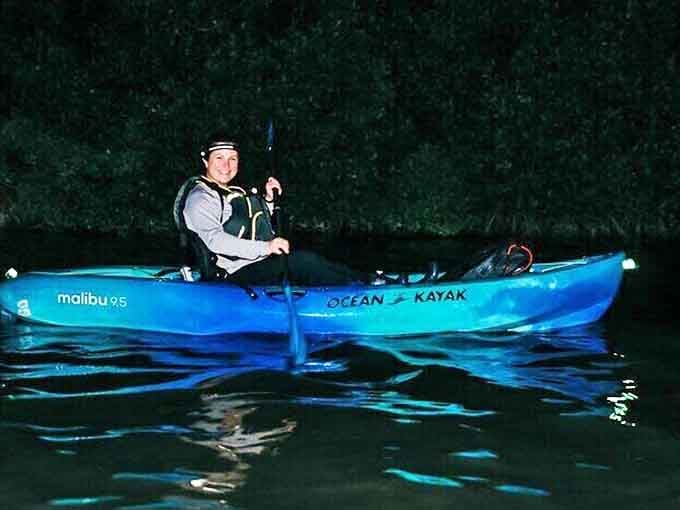 A paddler glides through the darkness, creating ripples of light that follow each stroke like aquatic fireflies dancing in their wake.