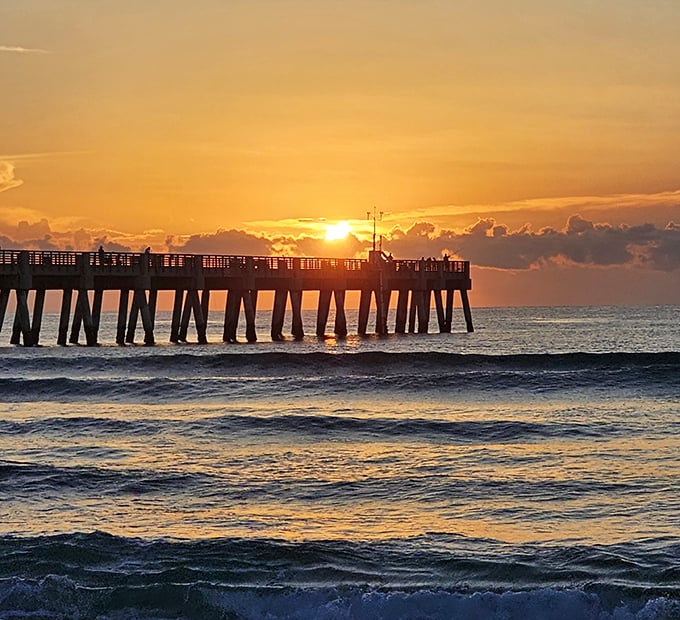 The day's final light bathes the pier in golden hues, as silhouetted figures savor the magic hour between day and night.