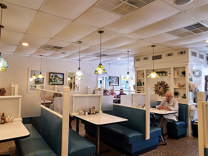 Classic diner booths in soothing teal create private sanctuaries for conversation, while stained glass pendant lights cast a warm glow that makes everyone look fabulous.