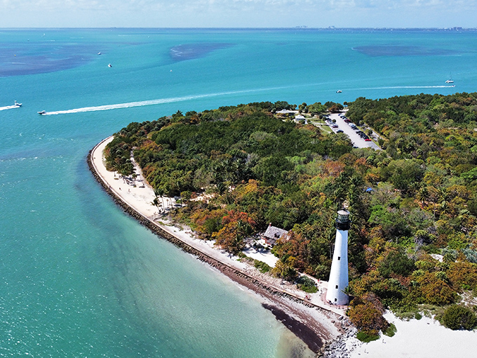 The historic lighthouse at Bill Baggs Cape Florida State Park stands tall against the blue sky, with palm trees swaying in the breeze.