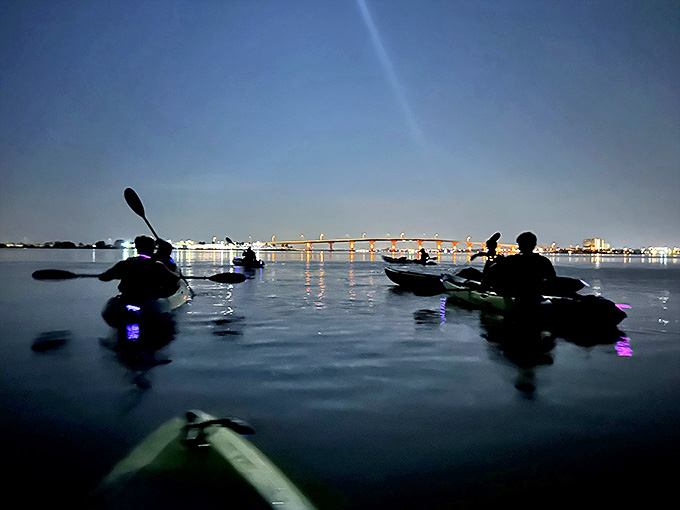 Kayakers drift beneath the Cocoa Beach bridge, their colorful safety lights creating a festive parade against the night skyline.