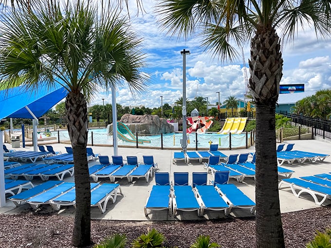 Blue lounge chairs await weary swimmers, arranged like a sea of comfort under colorful shade sails that battle Florida's relentless sunshine.