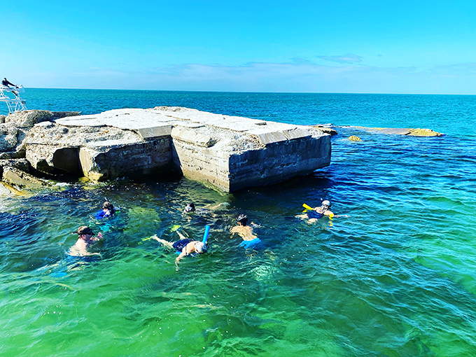 Concrete meets coral at this unique snorkeling spot where history and marine life converge. Swimmers explore the remnants of what appears to be an old structure now claimed by the sea.