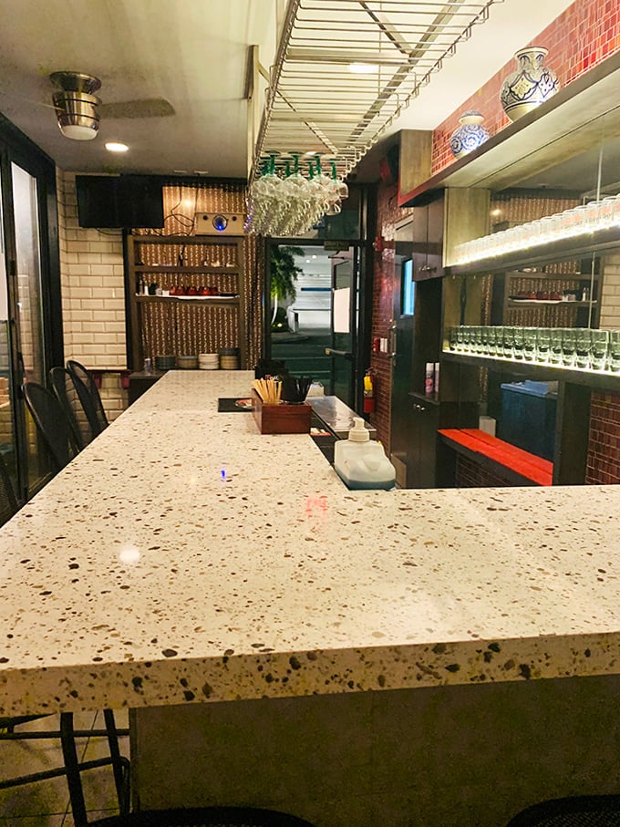 The bar counter gleams with possibility, a sleek modern stage where classic cocktails are reborn with theatrical flair and zero judgment for ordering something blue.