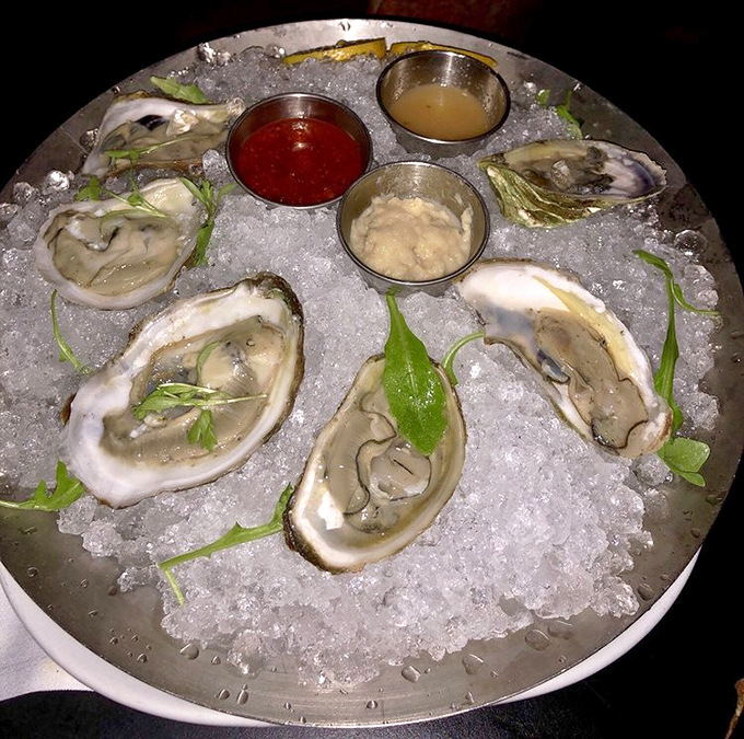 Fresh oysters nestled on ice like pearls in their shells, accompanied by three dipping sauces that enhance their briny perfection.