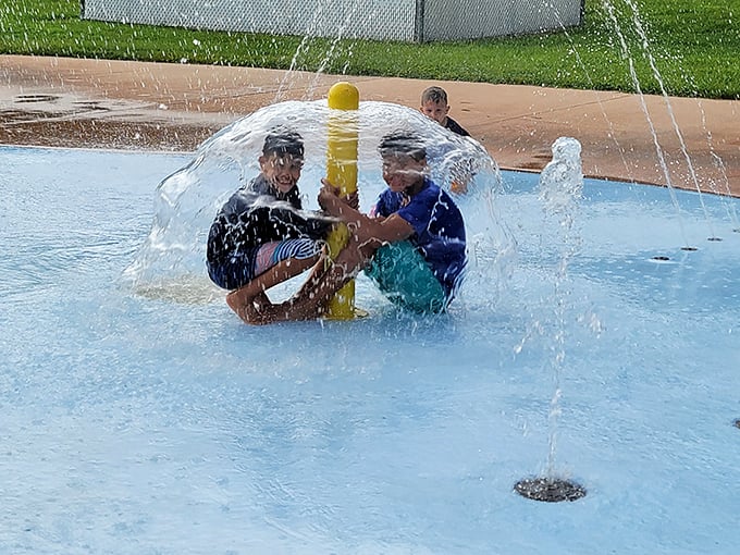 Two young adventurers discover the magic of water physics inside a dome fountain, their laughter amplified by their liquid enclosure.