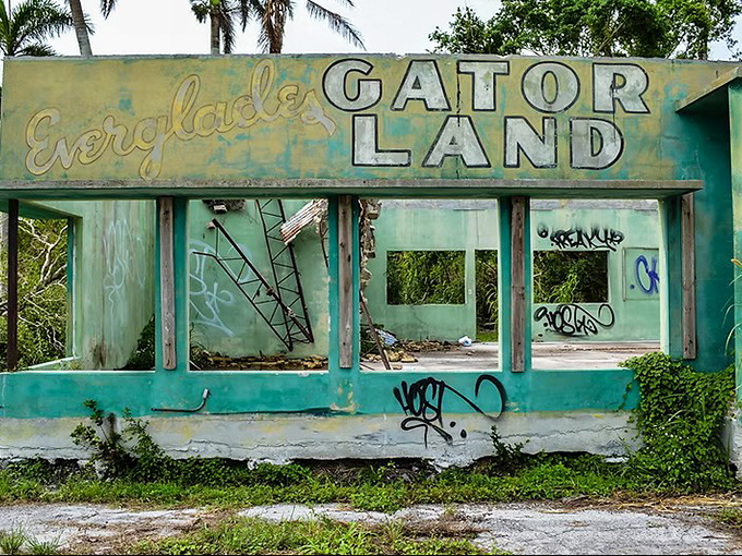 "Everglades Gator Land" announces itself in faded letters, a mint-green ghost from the era when roadside attractions lured station wagons with promises of reptilian thrills.