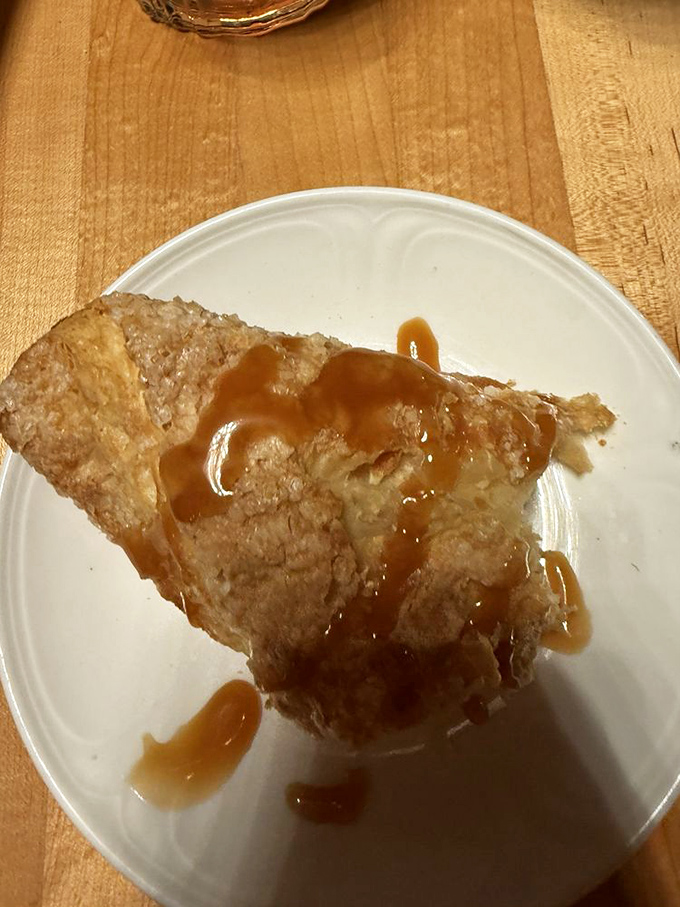 The apple turnover arrives warm and flaky, drizzled with caramel sauce that transforms this simple dessert into something worth confessing for.