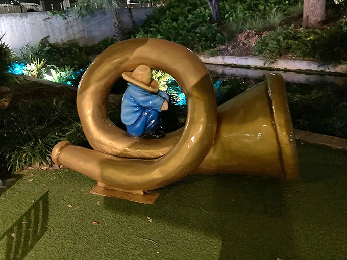 Little Boy Blue takes shelter inside his own instrument in this golden horn sculpture, a playful twist on the nursery rhyme.