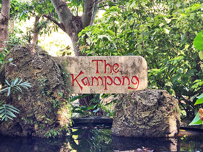 The Kampong's rustic stone marker emerges from tropical foliage, announcing your arrival to this hidden paradise with understated elegance.