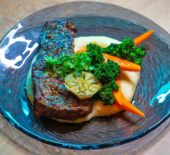A perfectly seared steak resting on cloud-like mashed potatoes, with vegetables standing at attention like colorful sentinels.