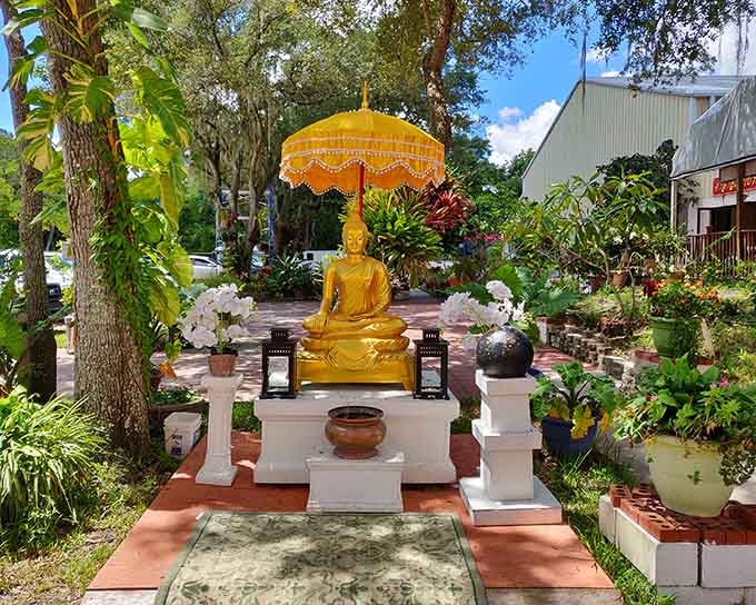 A golden Buddha sits in peaceful meditation, surrounded by flowers and offerings from devoted visitors seeking blessings.