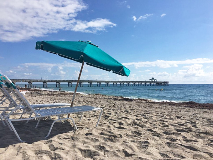 A quiet stretch of sandy beach invites relaxation, with calm waves and a long fishing pier in view.