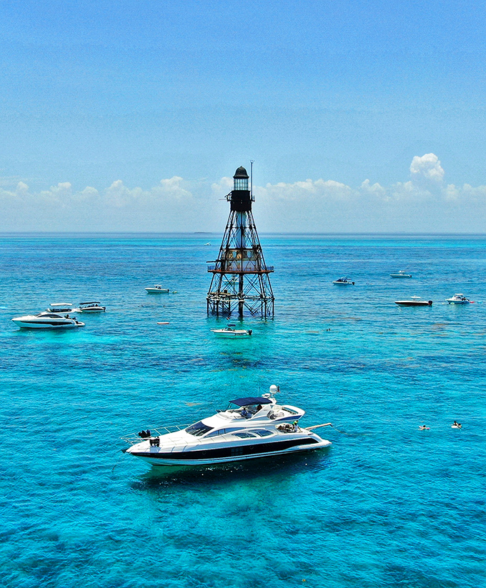 Fowey Rocks Lighthouse stands like a metal skeleton rising from turquoise waters, with luxury boats gathering around its base for the perfect Florida day.