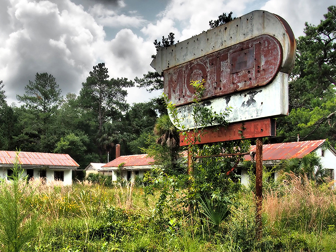 Nature slowly reclaims this forgotten motel, where the rusted sign stands like a tombstone marking the final resting place of road trip memories.