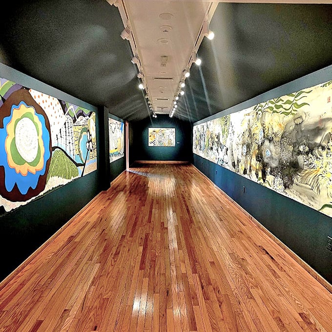 Polished wood floors reflect artistic visions along this gallery corridor, where dark walls make colors sing their visual symphony.