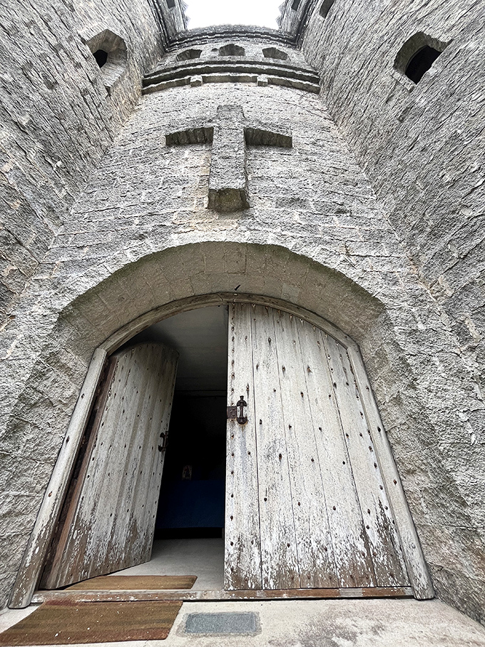 The weathered wooden doors swing open like a portal to another century, complete with stone cross guardian.