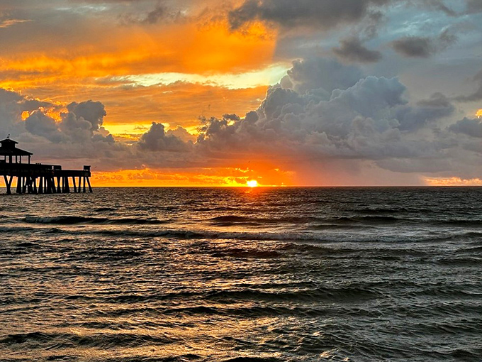 The fishing pier glows in silhouette as a breathtaking Florida sunset paints the sky in fiery colors.