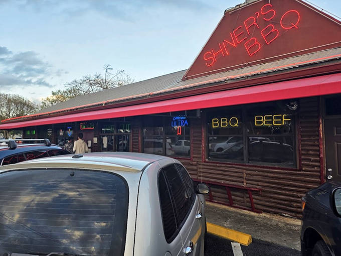 The log cabin-style exterior of Shiver's BBQ with its bright red awning stands ready to welcome hungry customers to a smoky flavor paradise.