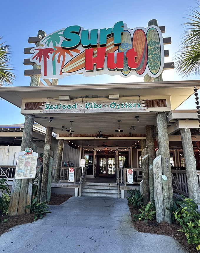 The welcoming entrance of The Surf Hut promises fresh seafood and beach vibes with its colorful surfboard sign and coastal decor.