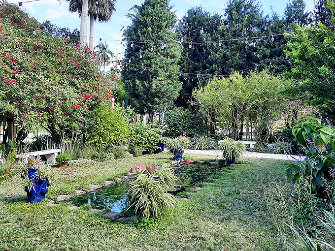 Lush greenery and a tranquil pond create a peaceful oasis between historic buildings, showcasing the native plants that early settlers would have known.