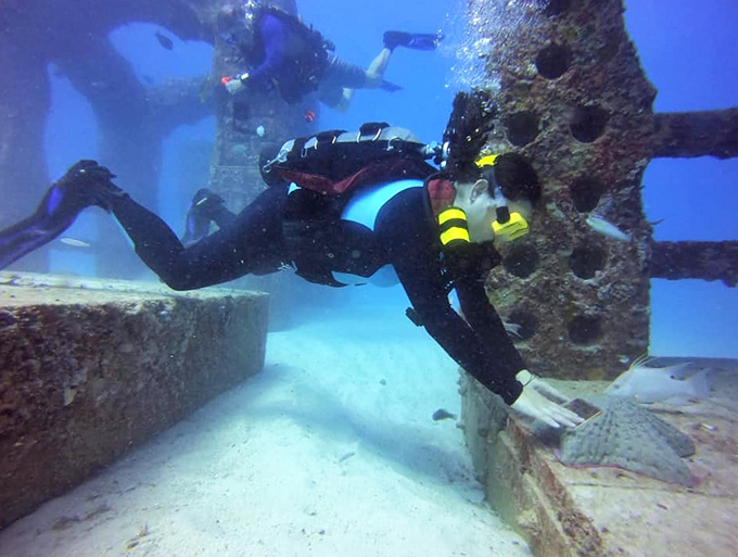 Divers explore the structures with reverent curiosity, their bubbles rising like ephemeral prayers through this underwater city of remembrance.