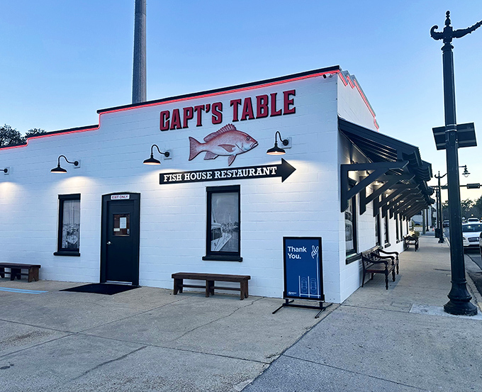 Captain's Table's crisp white exterior with bold red signage stands out against the blue Florida sky. Black awnings provide welcome shade for outdoor diners.