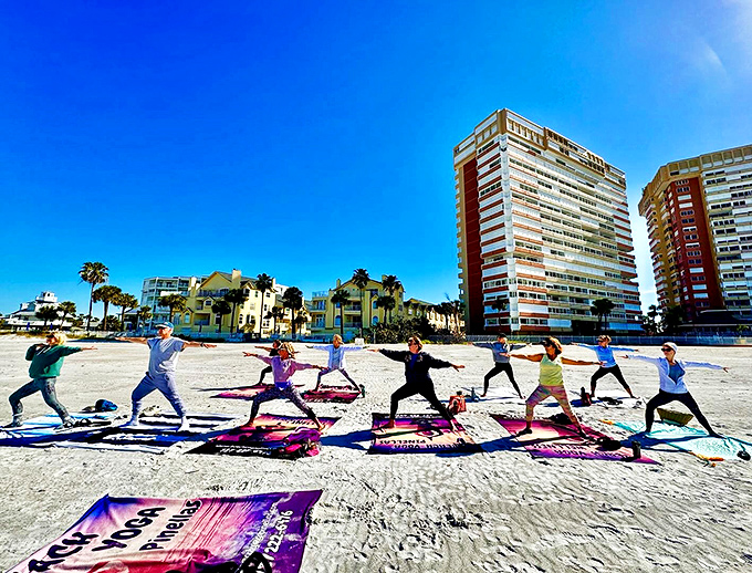 Colorful yoga mats line the pristine white sands of St. Pete Beach, where participants stretch toward the sky with high-rise condos creating a unique urban-meets-nature backdrop.