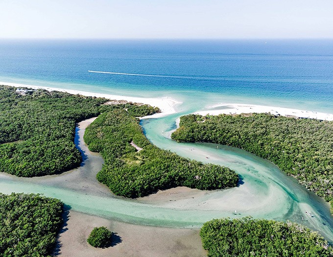 Aerial view of Clam Pass reveals nature's artistry &ndash; a winding teal waterway embraced by lush mangroves meeting the Gulf's endless blue horizon.