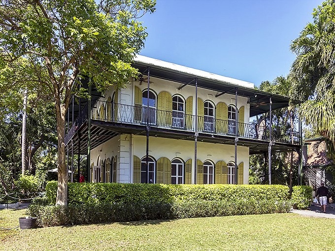 The iconic yellow facade of Hemingway's Key West sanctuary stands proudly among swaying palms, a literary landmark where stories and six-toed cats roam freely.