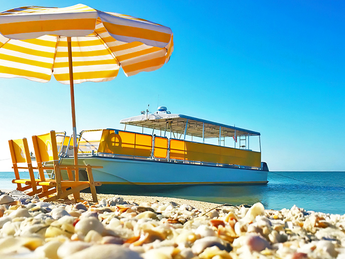 The bright yellow ferry awaits its passengers, ready to transport shell-hunters to paradise while the striped umbrella stands guard over empty beach chairs.