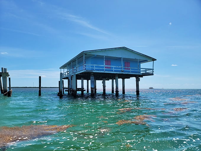 A weathered blue stilt house stands defiantly in turquoise waters, like a stubborn old-timer who refuses to leave his favorite fishing spot.