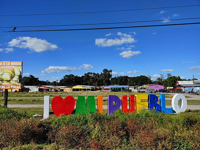 The colorful "I ❤ MI PUEBLO" sign stands as a cheerful sentinel, welcoming visitors to this vibrant marketplace experience.