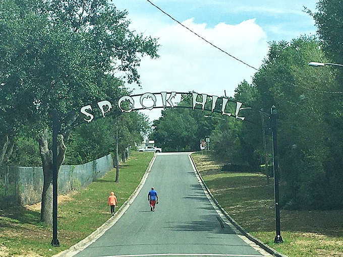 Pedestrians stroll beneath the Spook Hill sign, enjoying this quirky attraction that has bewildered and delighted visitors for generations.