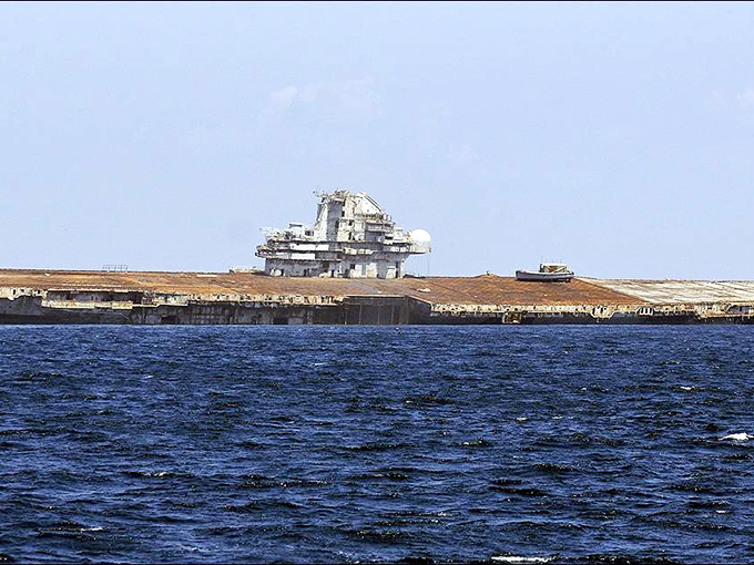 The carrier's massive profile cuts through Gulf waters, its flight deck now serving as nature's landing strip for schools of fish.