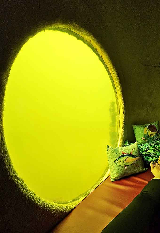 The bedroom's circular window glows with an otherworldly yellow-green light, framing the aquatic world beyond like a living painting.