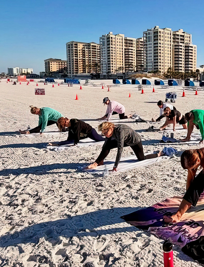 Participants in downward dog create a human wave of concentration, their forms silhouetted against the sand while high-rise buildings watch from afar.