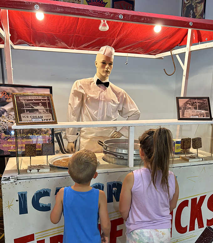 Young visitors peer into a vintage ice cream stand, complete with a mannequin vendor ready to serve up nostalgic treats from carnival days past.