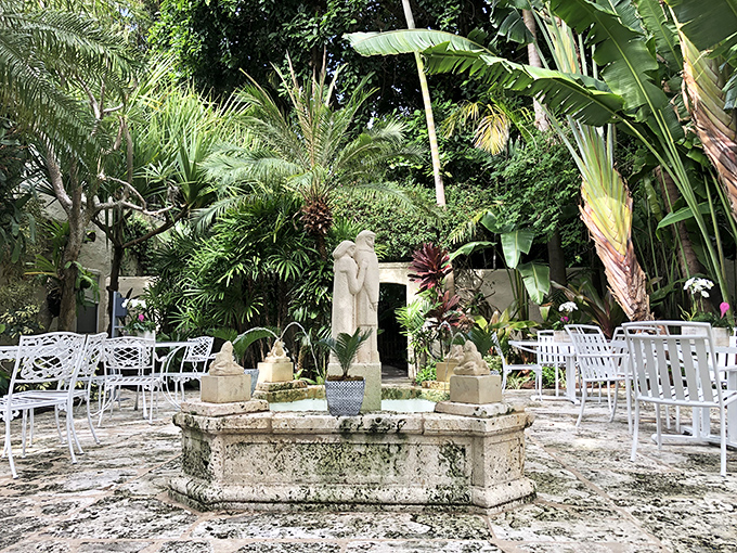 White garden furniture creates an intimate gathering space around a weathered stone fountain &ndash; perfect for contemplative afternoon chats.