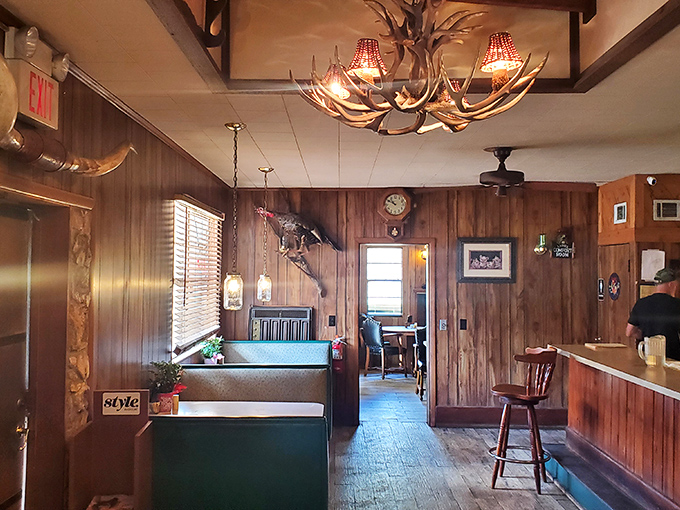 Antler chandeliers cast a warm glow over wood-paneled walls, creating an atmosphere where hunting lodge meets fine dining with unpretentious charm.