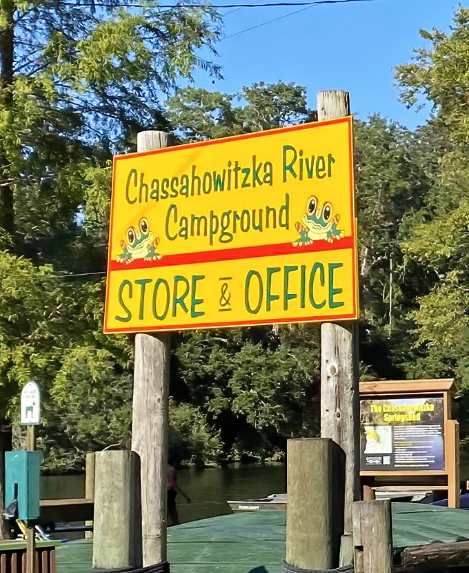 The cheerful campground sign welcomes adventurers with a promise of simple pleasures and natural wonders just beyond the dock.